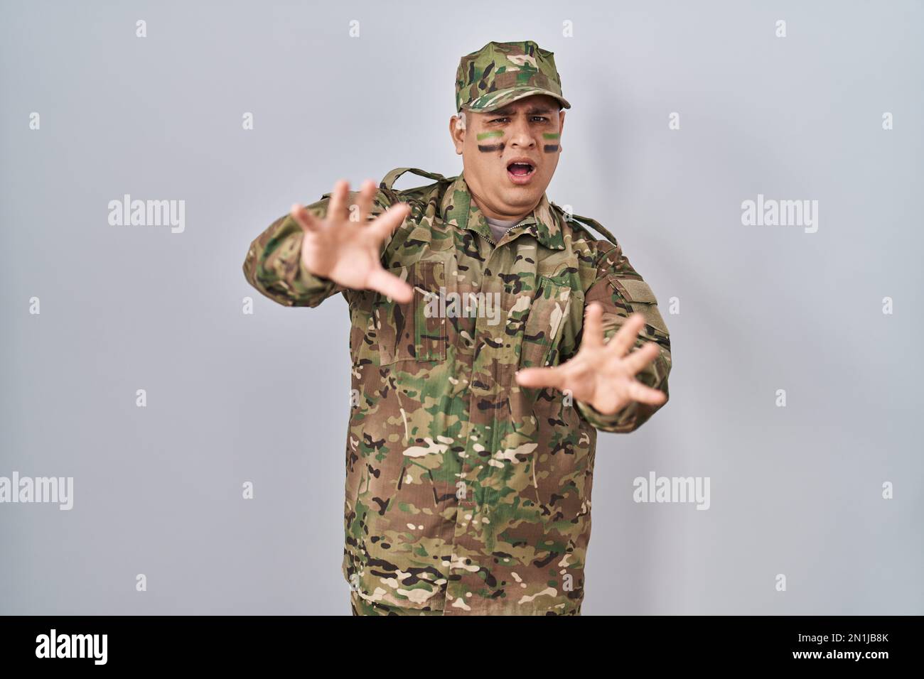 Hispanic young man wearing camouflage army uniform afraid and terrified ...