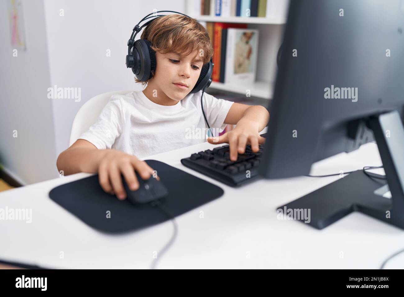 Adorable caucasian boy student using computer sitting on table at ...
