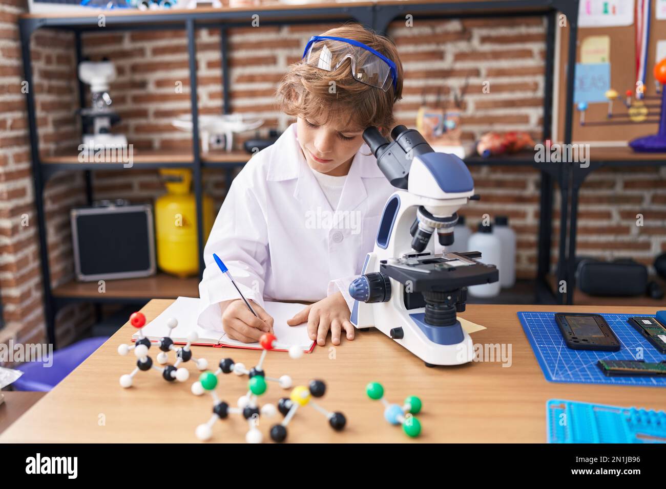 Adorable caucasian boy student using microscope writing on notebook at ...
