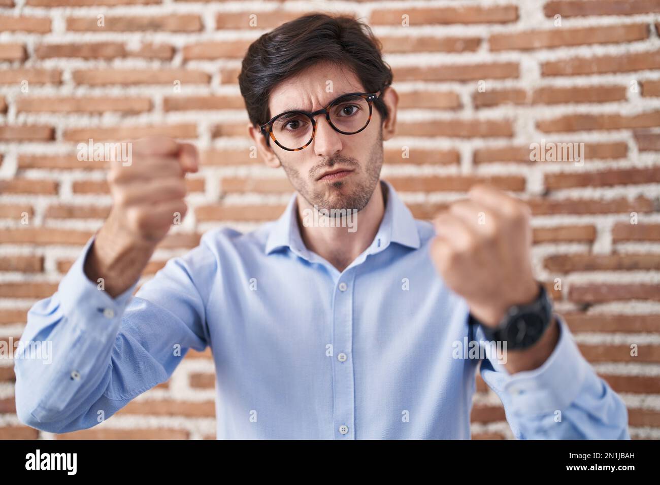 Young hispanic man standing over brick wall background angry and mad ...