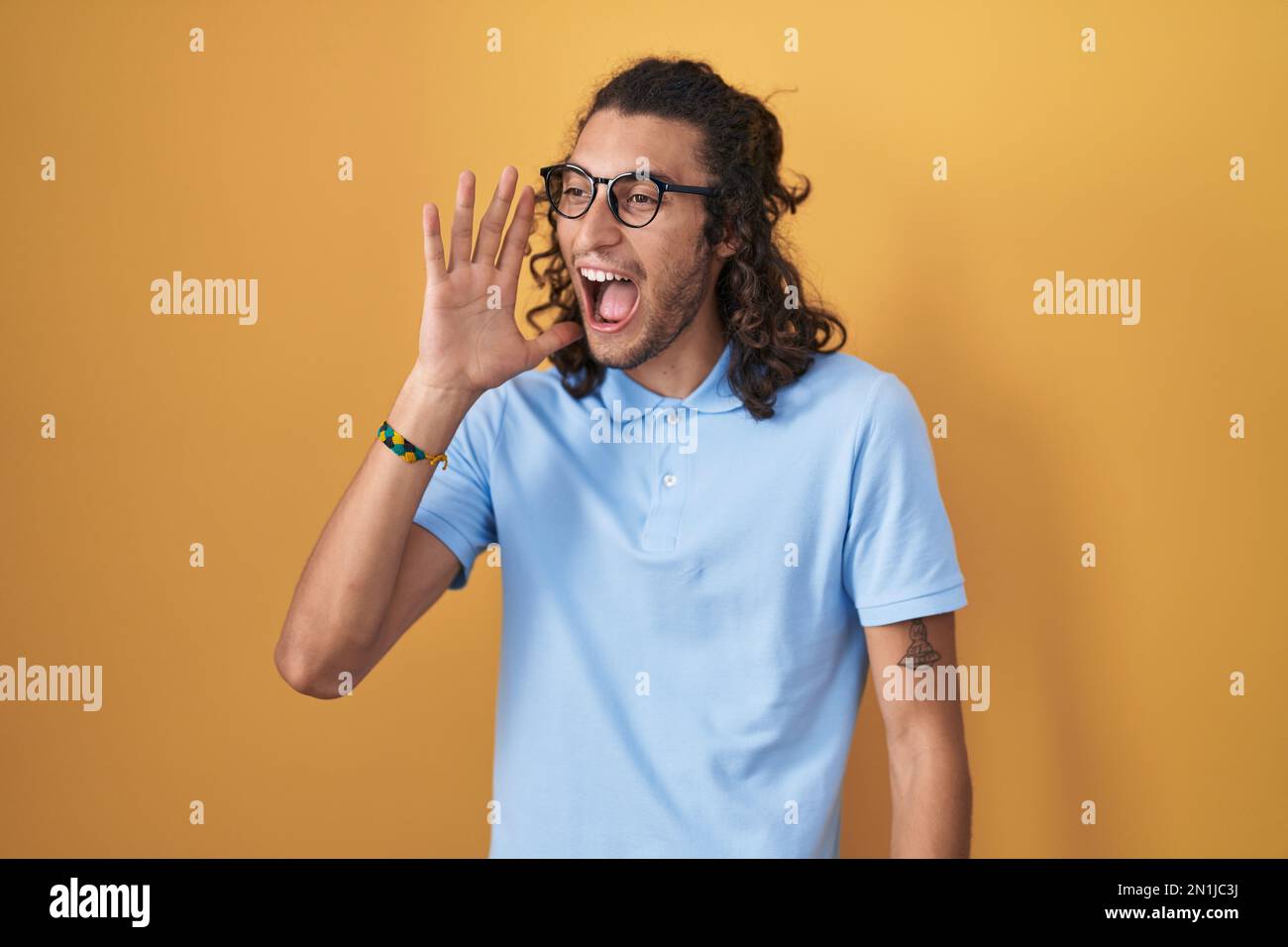 Young hispanic man standing over yellow background shouting and ...