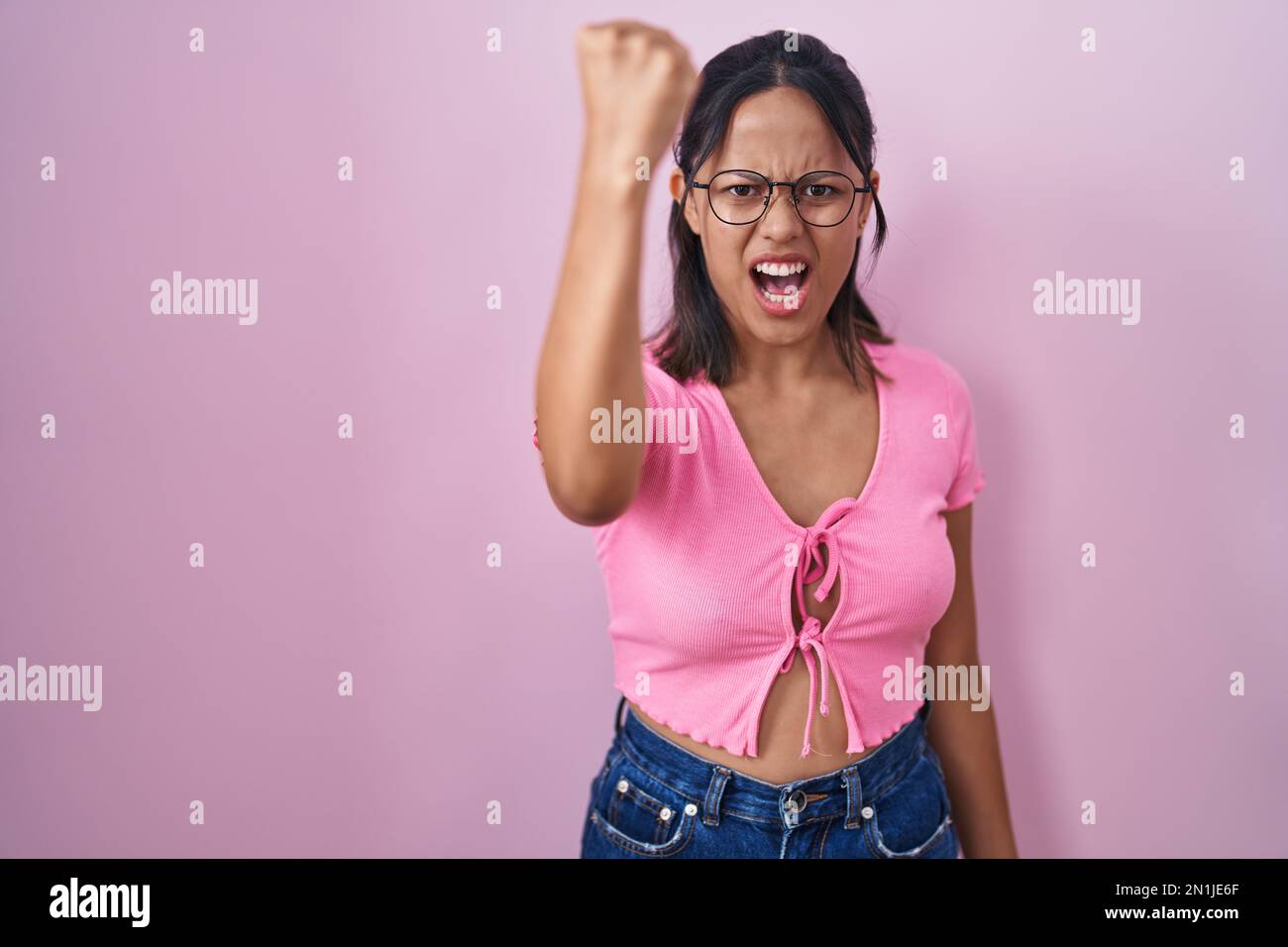 Hispanic young woman standing over pink background wearing glasses ...