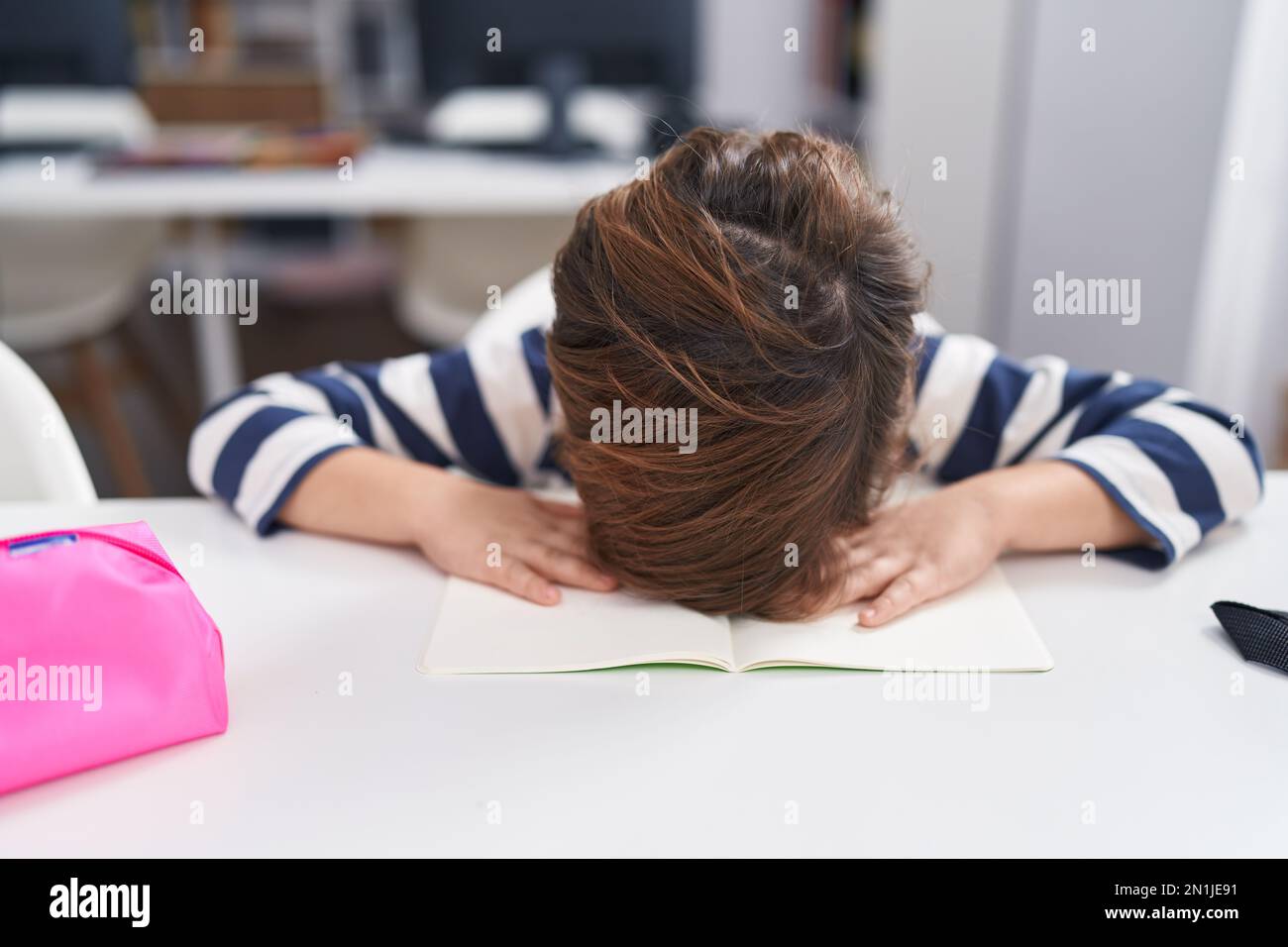 Adorable hispanic boy student with head on table stressed at classroom ...