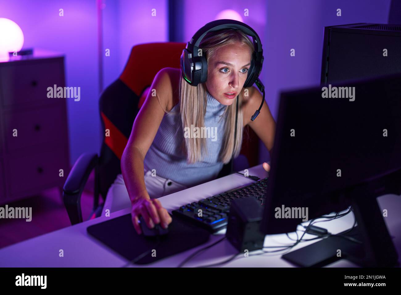 Young blonde woman streamer playing video game using computer at gaming ...