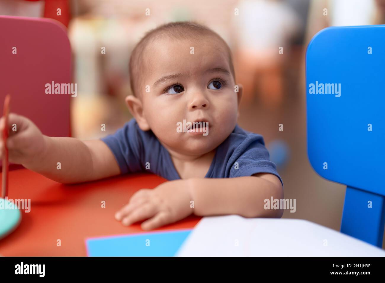 Adorable chinese toddler leaning on table standing at kindergarten ...