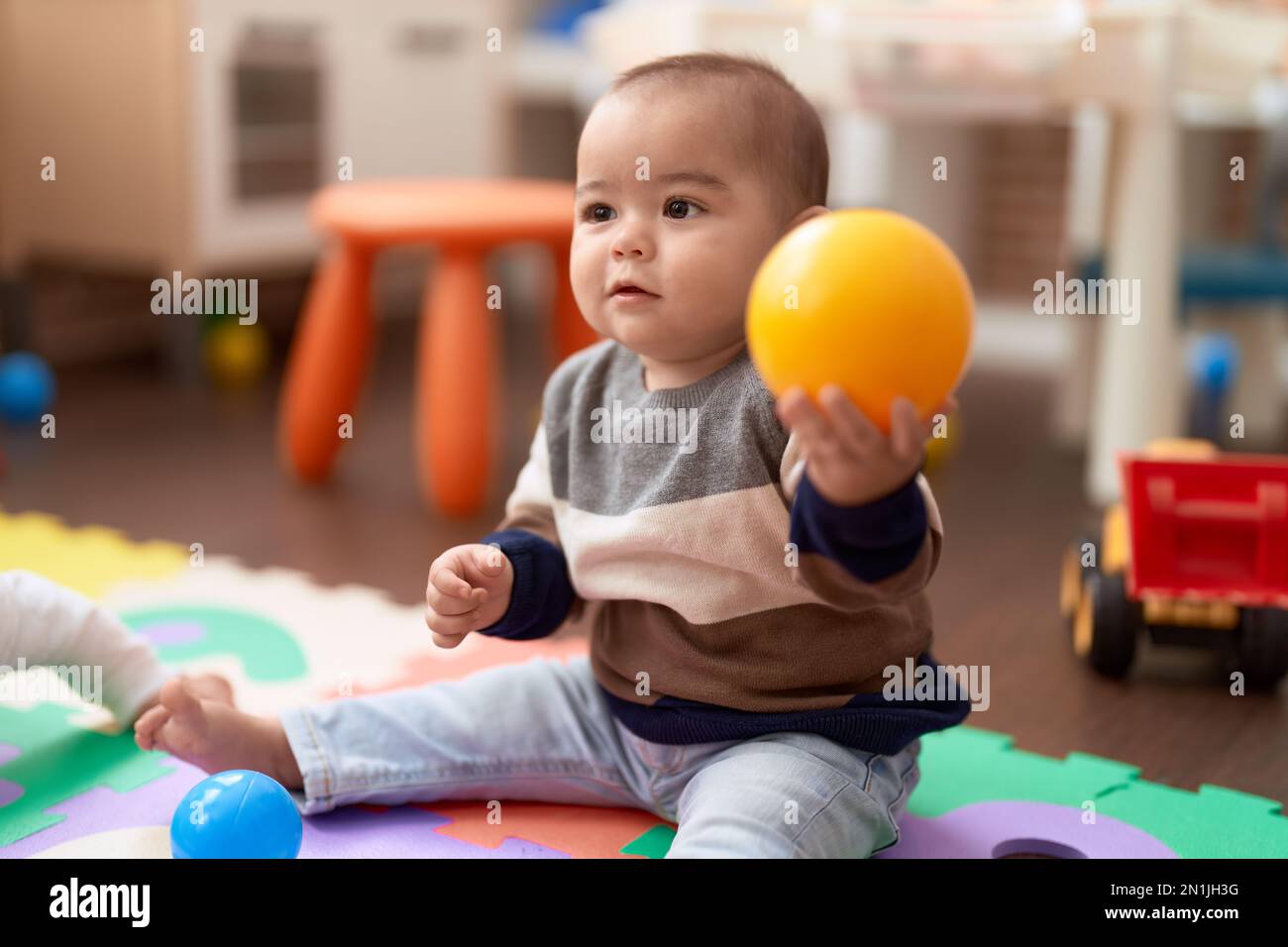 Adorable chinese toddler playing with ball sitting on floor at ...