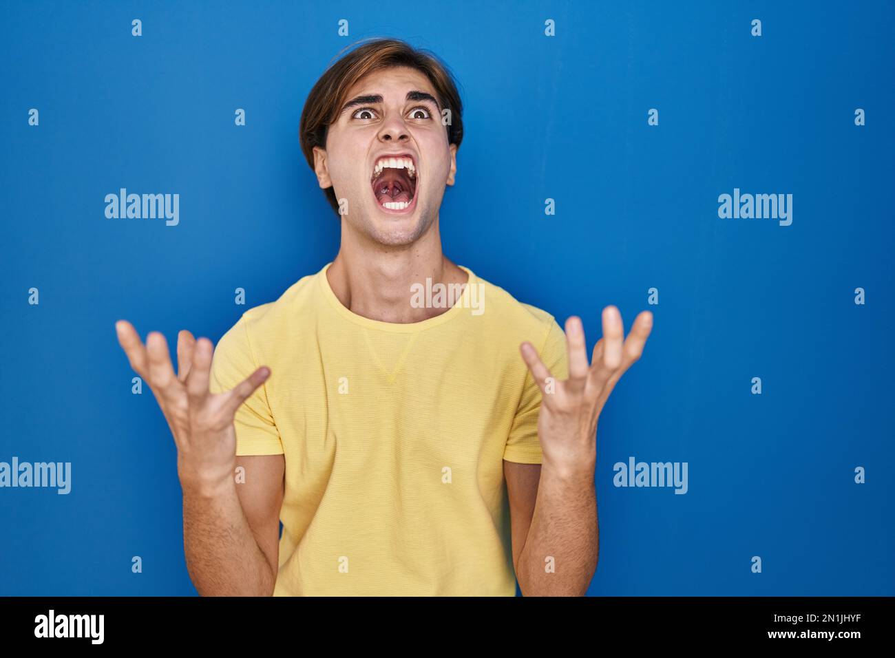 Young man standing over blue background crazy and mad shouting and ...