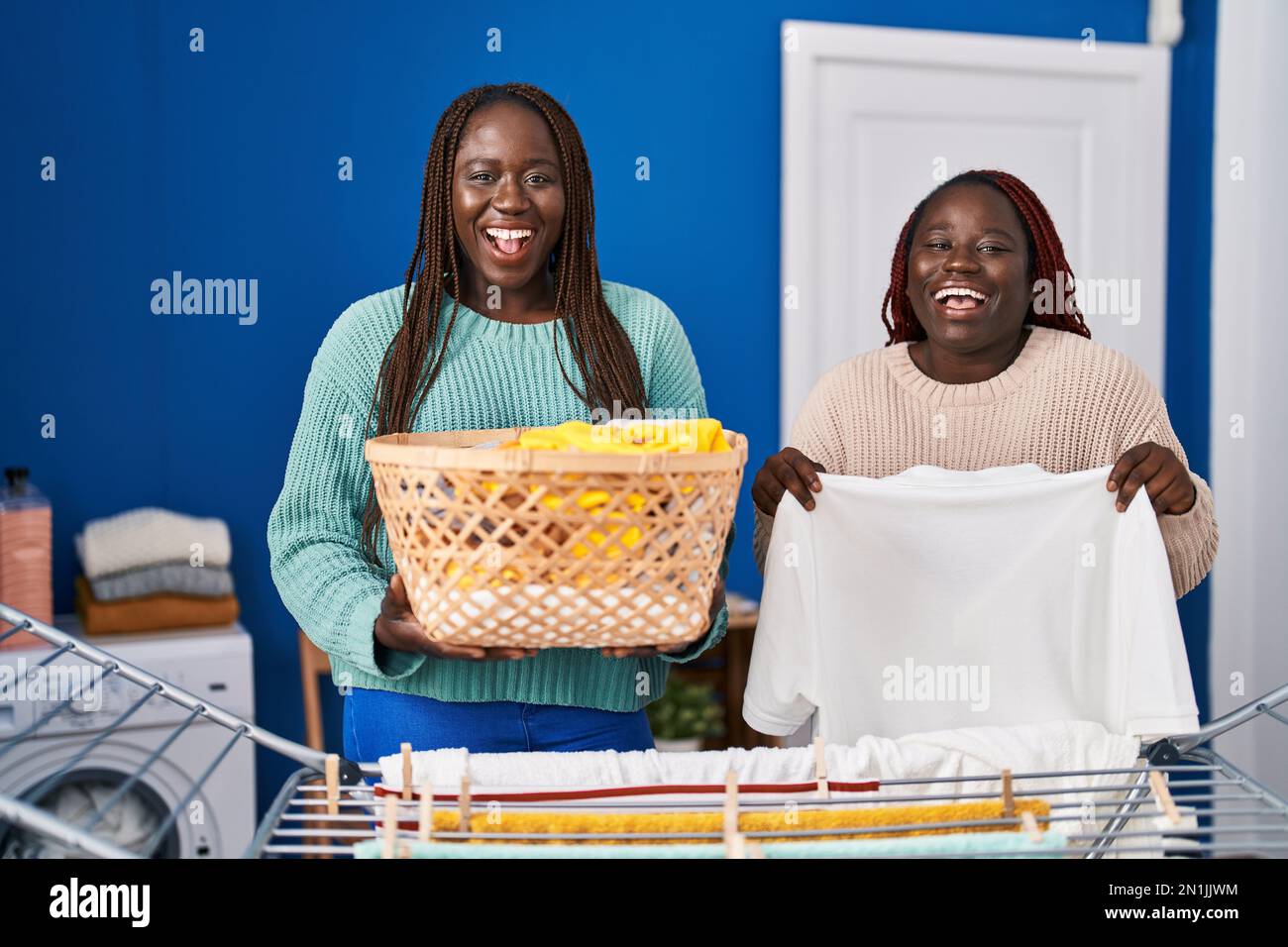 Two african women hanging clothes at clothesline smiling and laughing ...