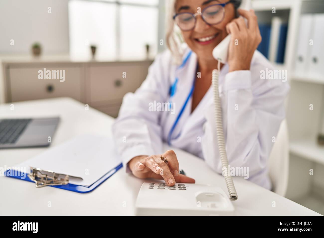 Middle age woman wearing doctor uniform talking on the telephone at ...