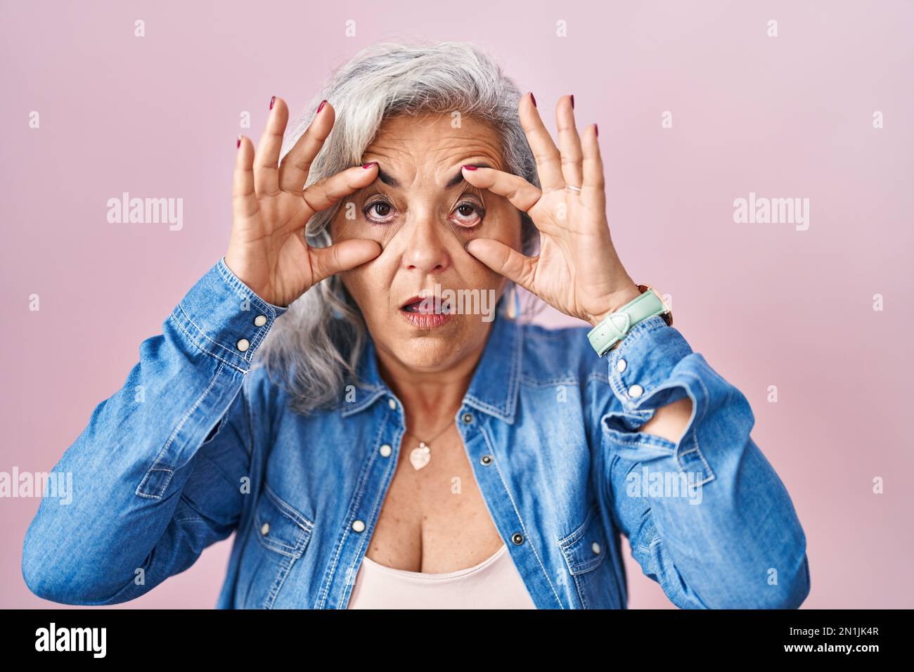 Middle age woman with grey hair standing over pink background trying to ...