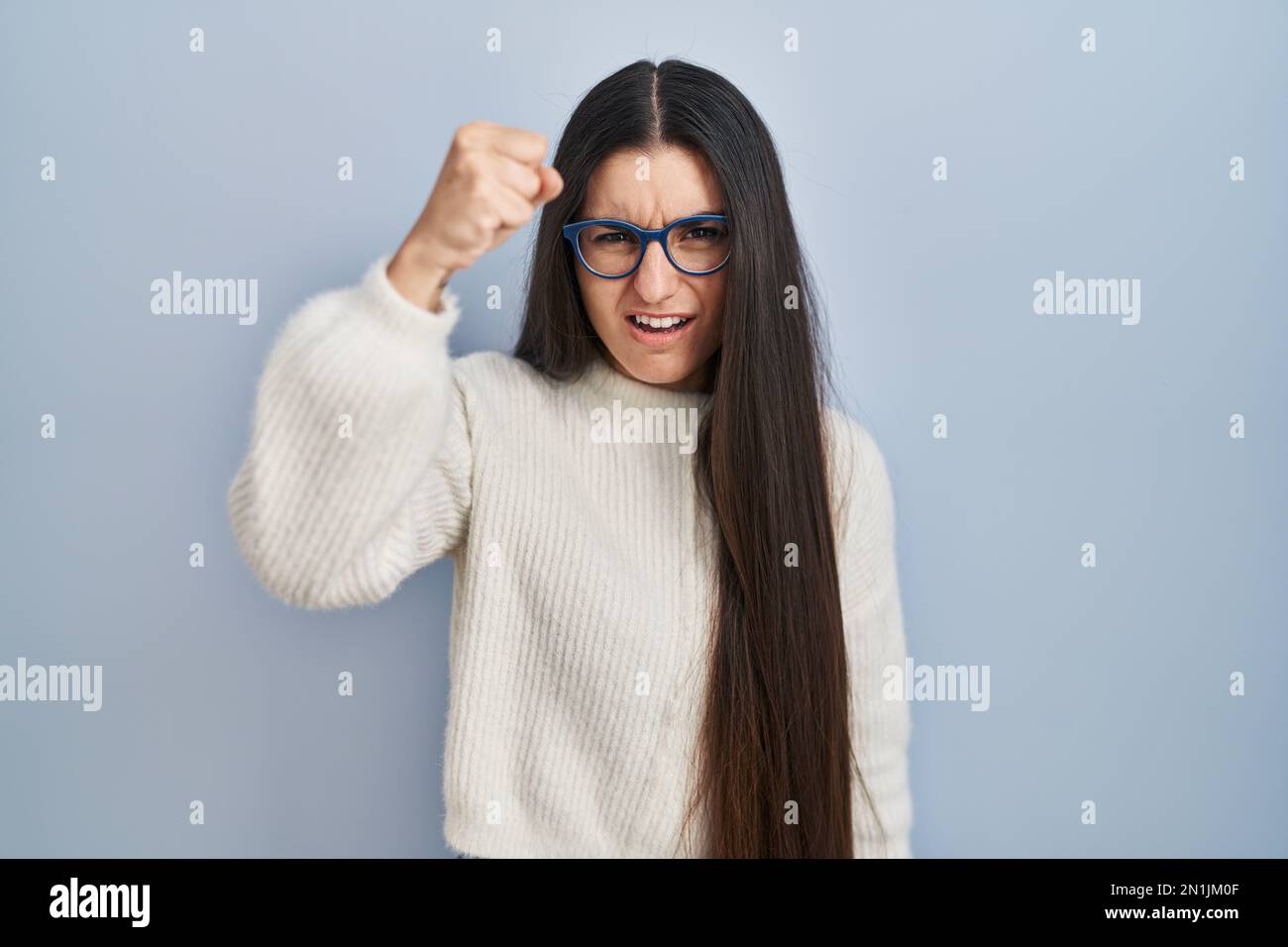 Young hispanic woman wearing casual sweater over blue background angry ...