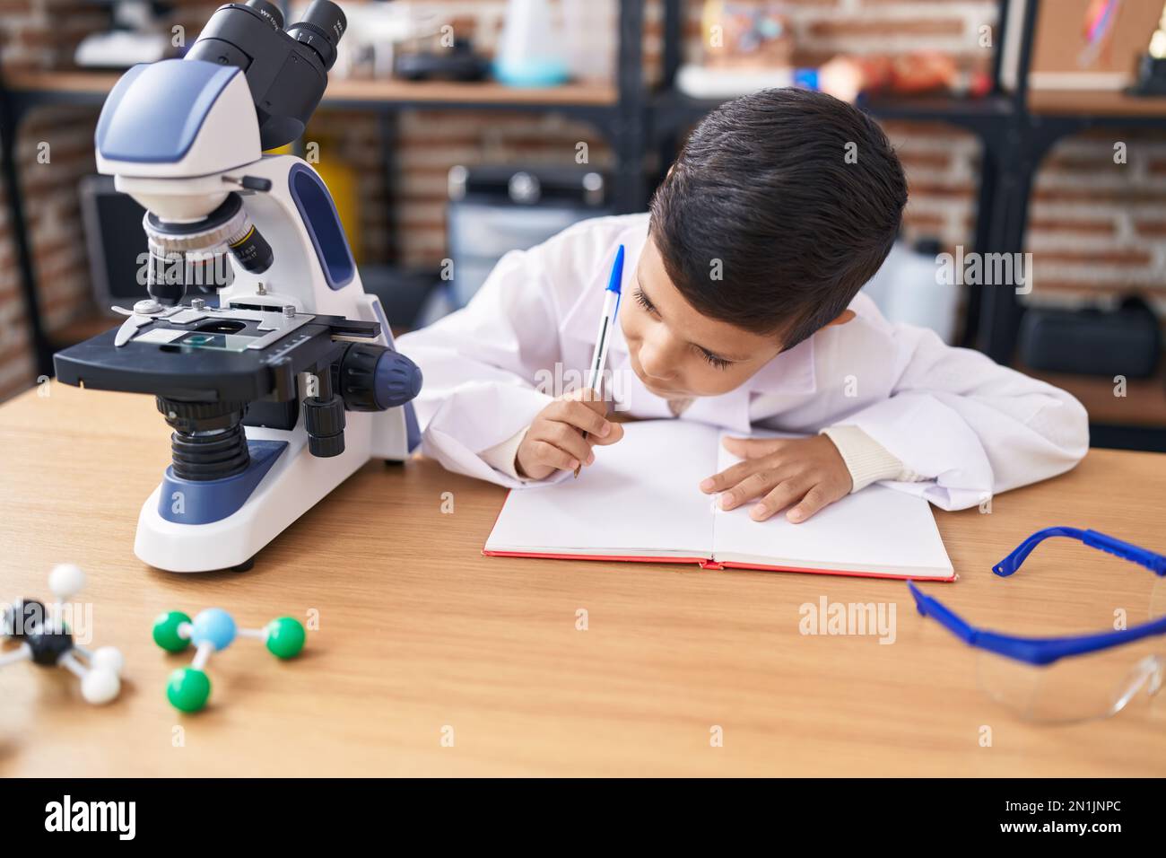 Adorable hispanic boy student using microscope writing on notebook at ...