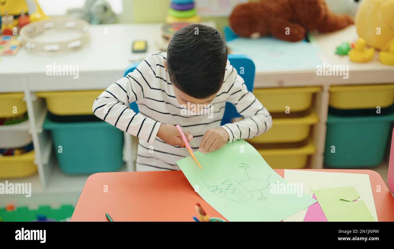 Adorable hispanic boy student cutting paper at kindergarten Stock Photo ...