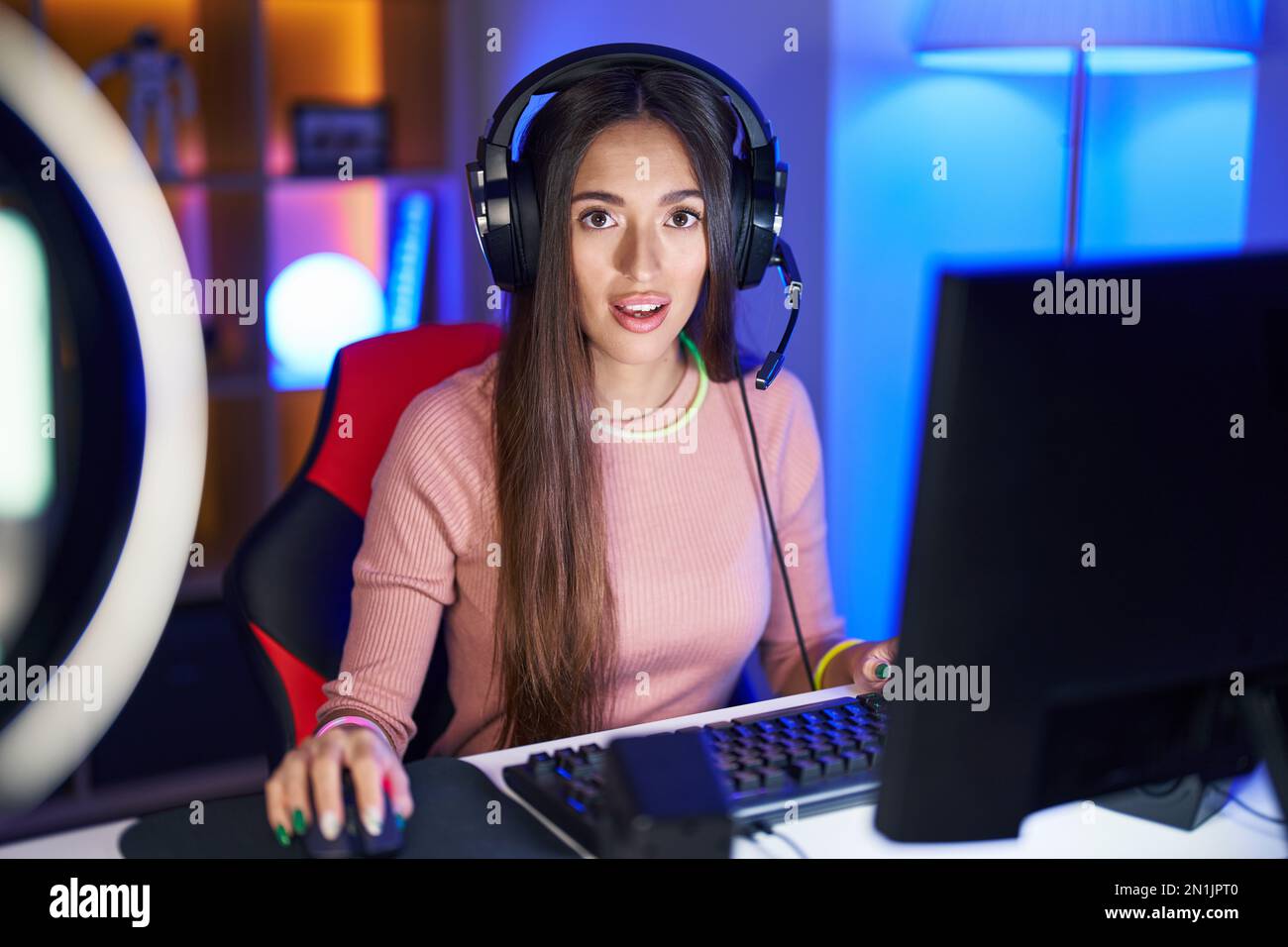 Young hispanic woman playing video games afraid and shocked with ...