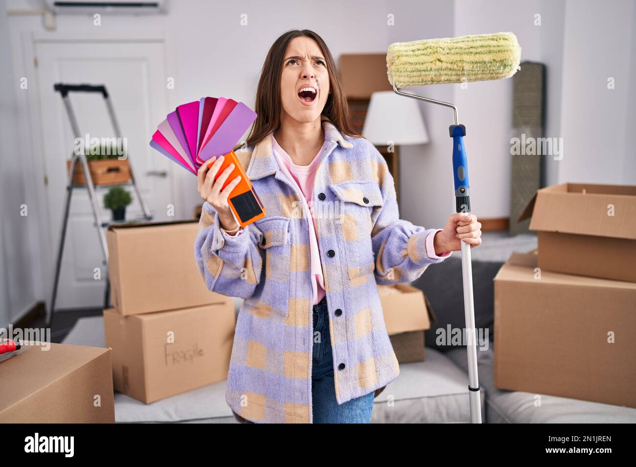 Young brunette woman painting new home walls with paint roller angry ...