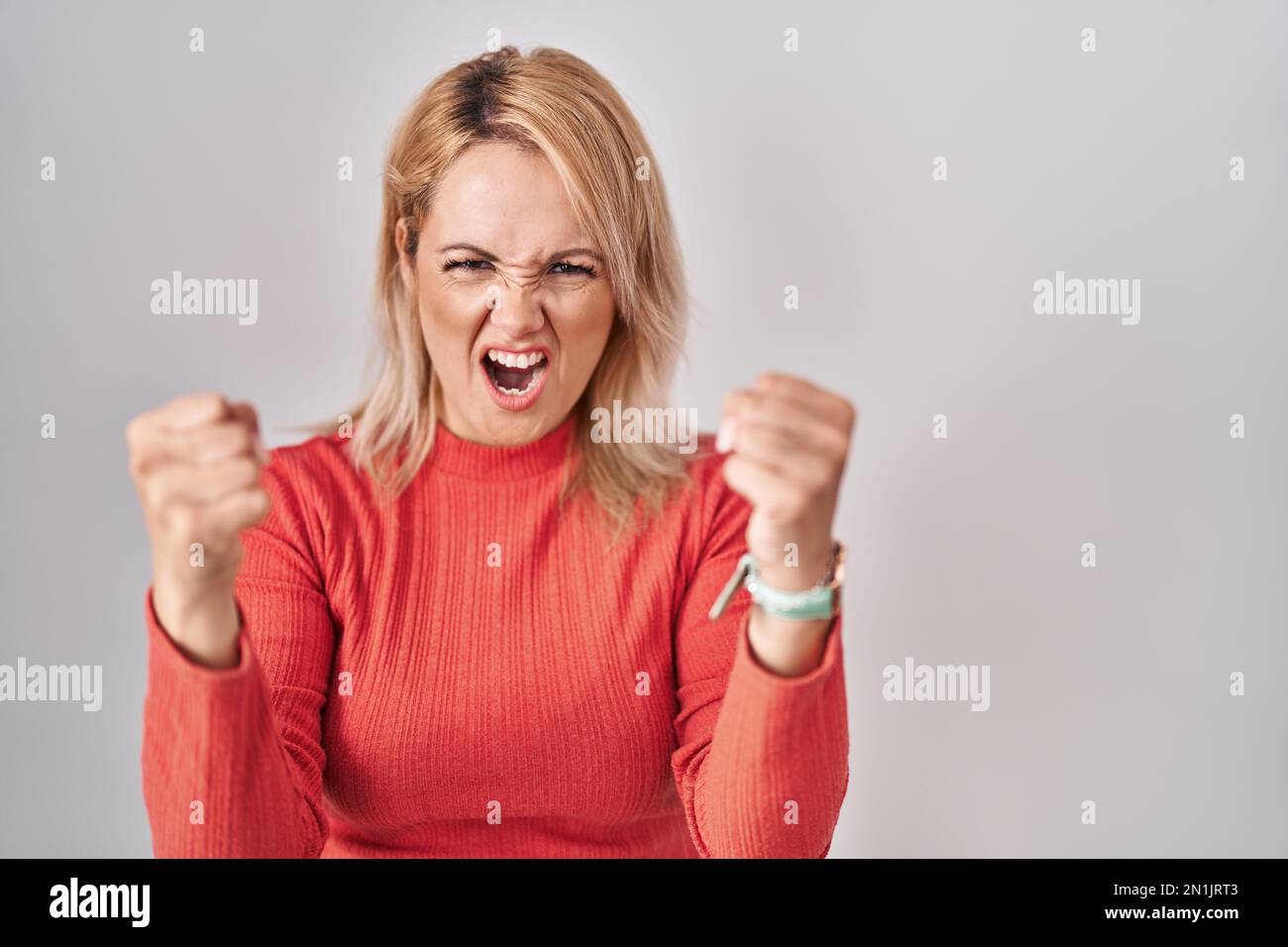 Blonde woman standing over isolated background angry and mad raising ...
