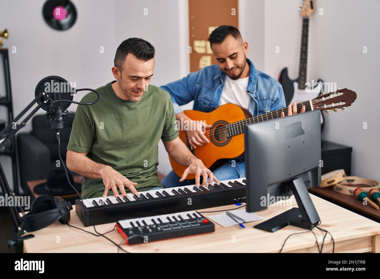 Two men musicians playing piano and classical guitar at music studio ...