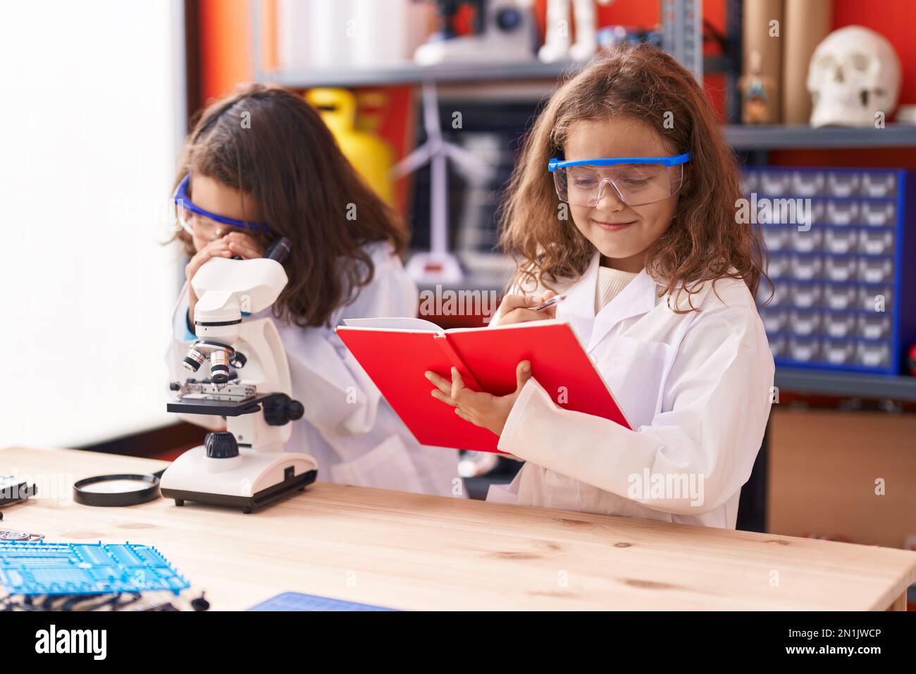 Two kids students using microscope writing on notebook at laboratory ...