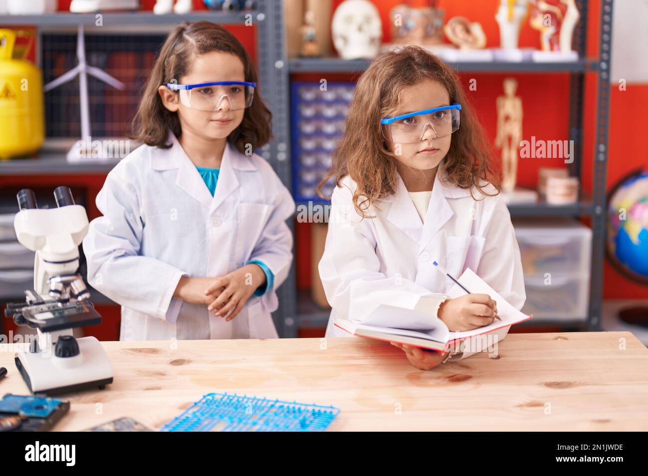 Two kids students using microscope writing on notebook at kindergarten ...