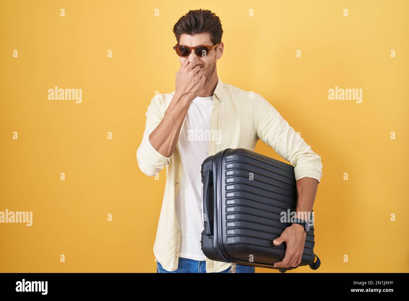 Young hispanic man holding suitcase going on summer vacation smelling ...