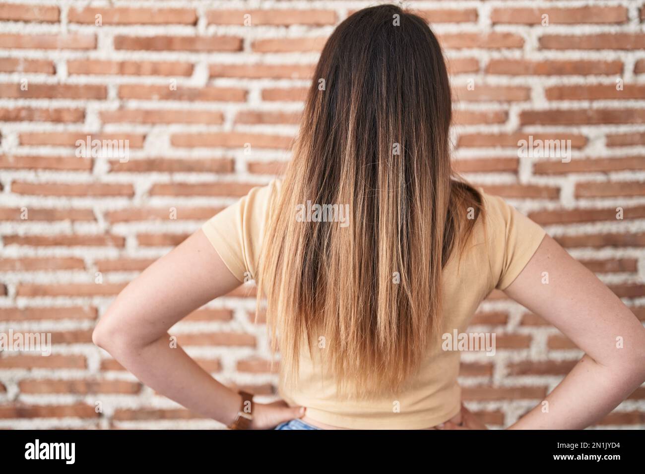 Young brunette woman standing over bricks wall standing backwards ...