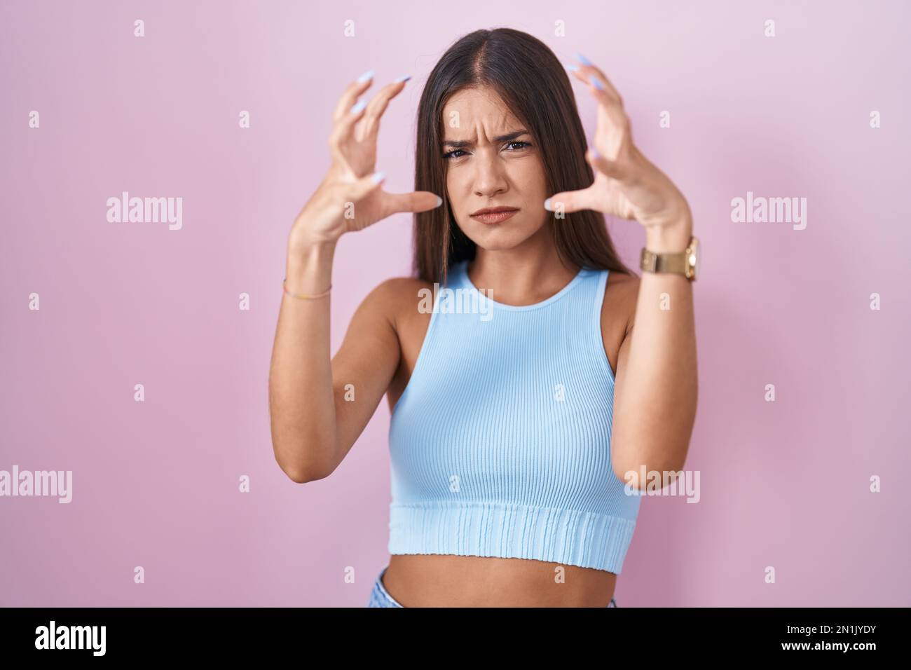 Young brunette woman standing over pink background shouting frustrated ...