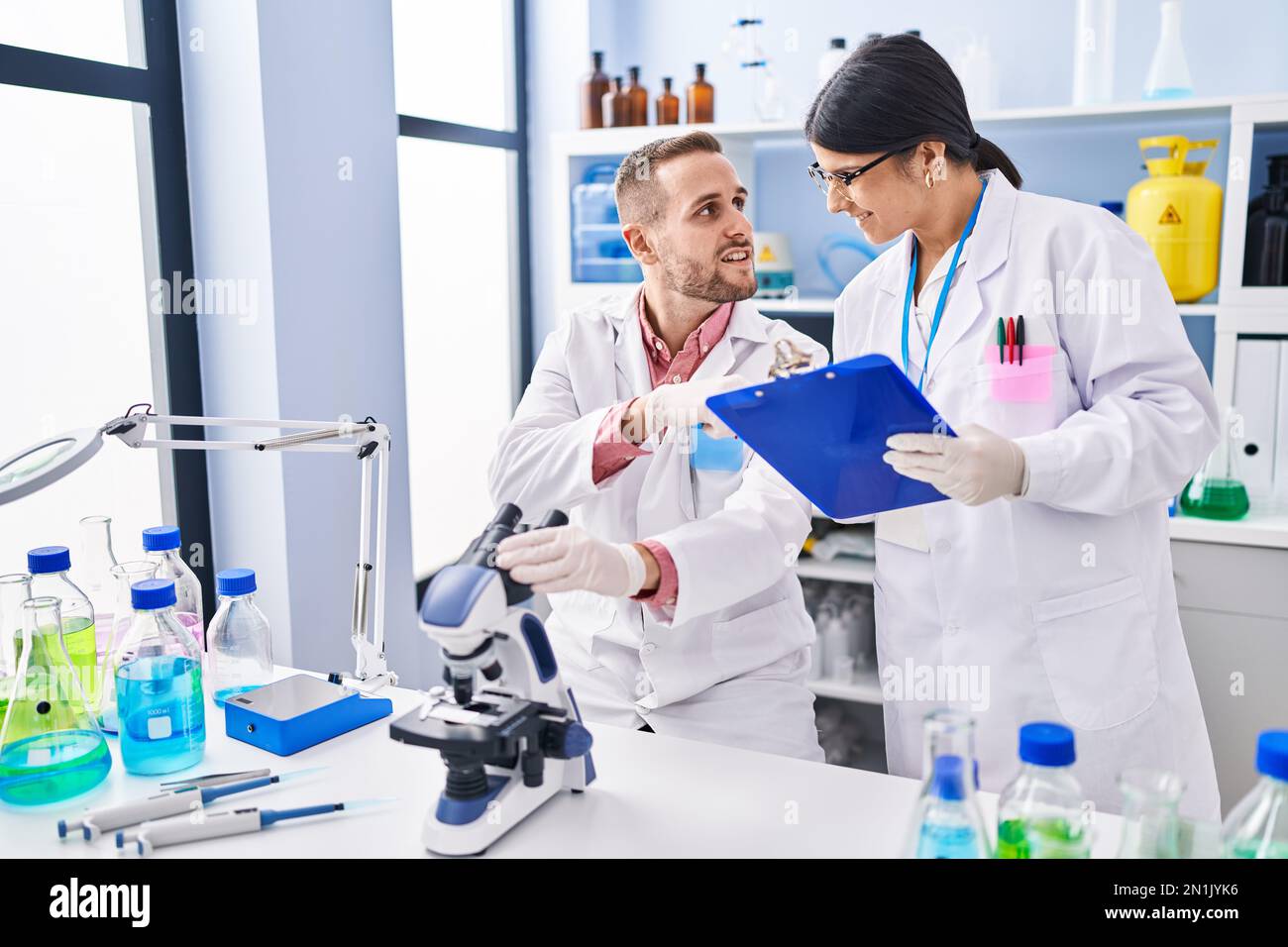 Man and woman wearing scientists uniform using microscope at laboratory ...