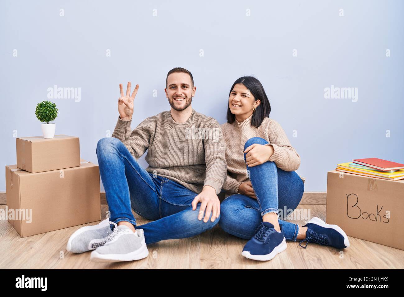 Young couple moving to a new home showing and pointing up with fingers ...