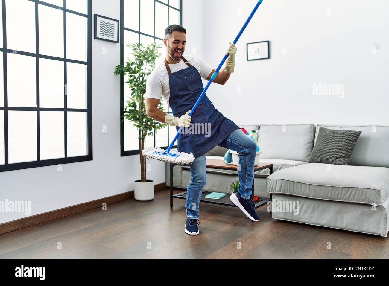 Young hispanic man cleaning floor and singing song using mop as a ...