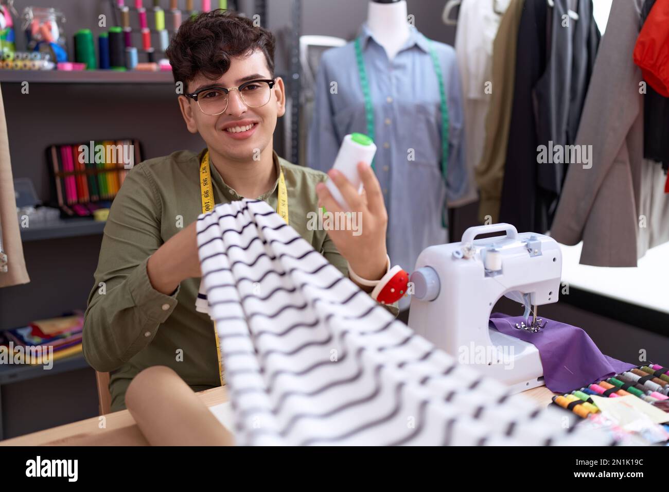 Non binary man tailor smiling confident holding cloth and thread at ...