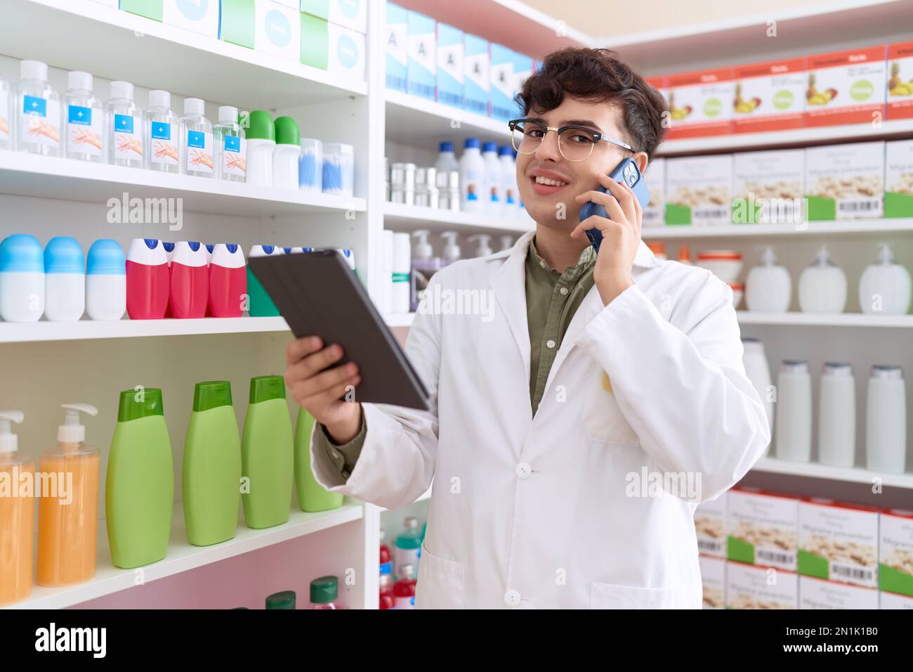Non binary man pharmacist using touchpad talking on smartphone at ...