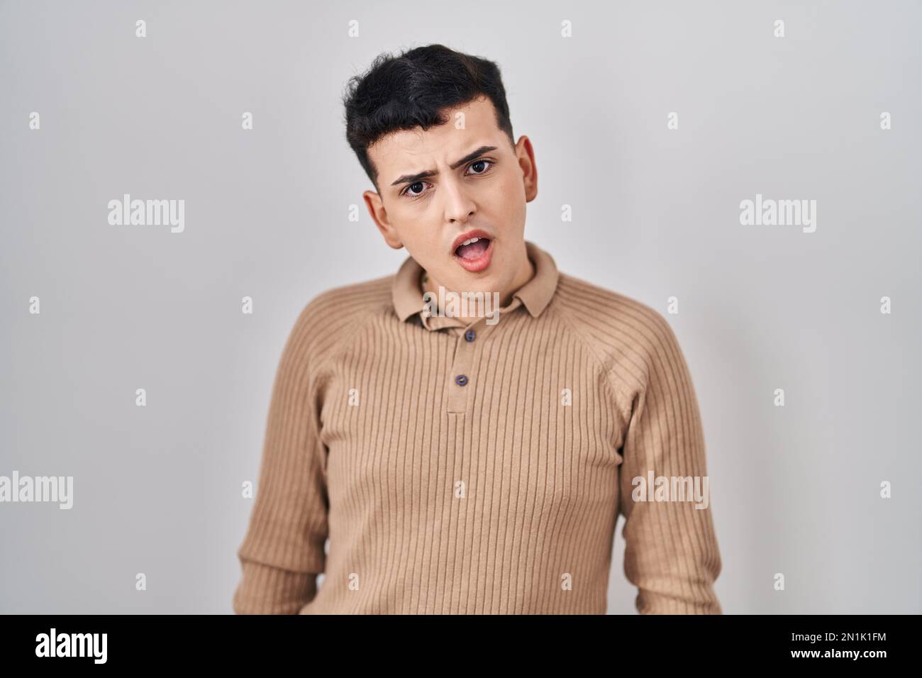 Non binary person standing over isolated background in shock face ...