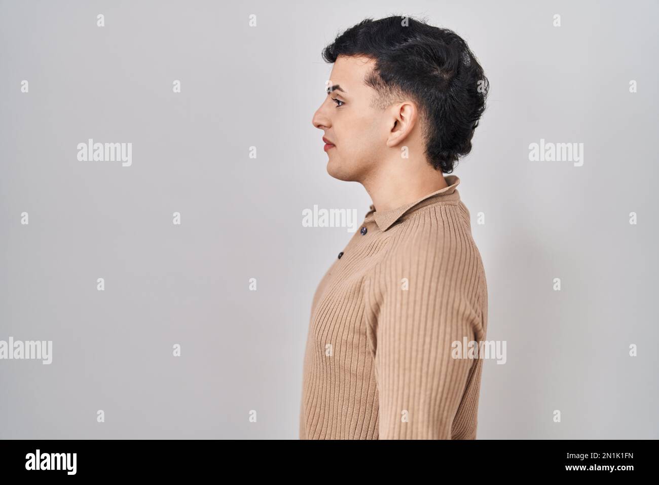 Non binary person standing over isolated background looking to side ...