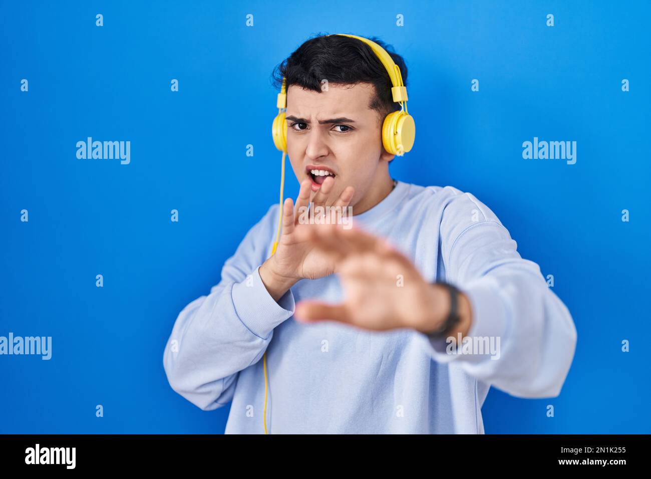 Non binary person listening to music using headphones afraid and terrified with fear expression ...