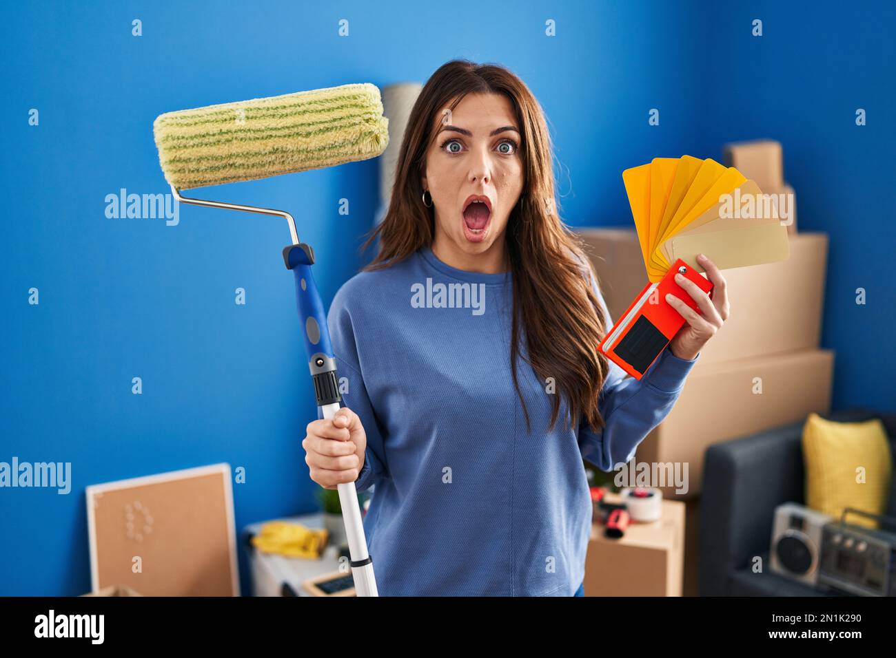 Young brunette woman holding roller painter painting new house in shock ...
