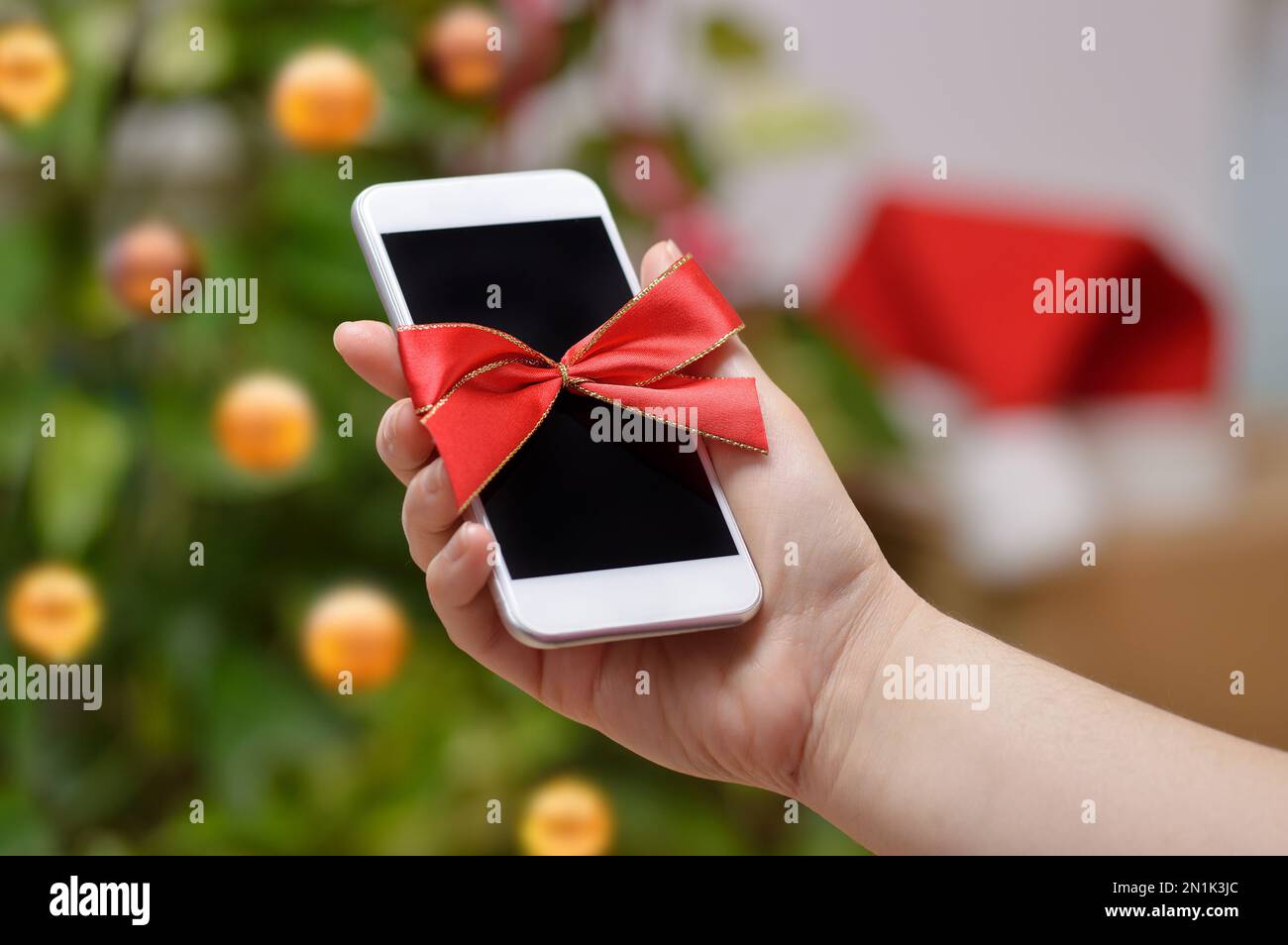 Hand showing a smart phone with a Christmas tree background at home ...