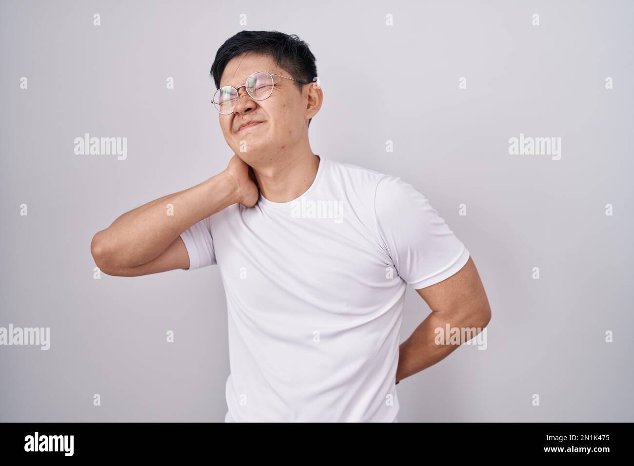 Young asian man standing over white background suffering of neck ache ...