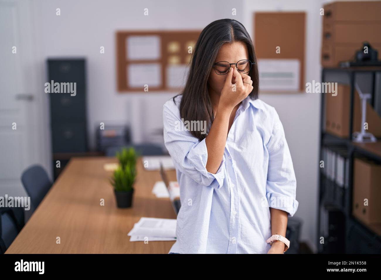 Young hispanic woman at the office tired rubbing nose and eyes feeling ...