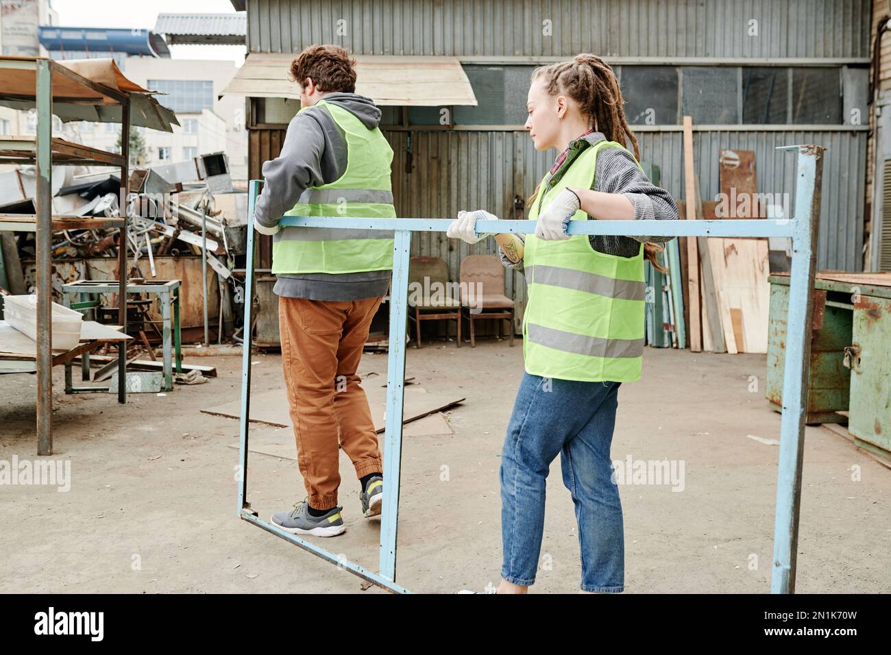 Scrapyard workers carrying big metal frame to pile Stock Photo - Alamy