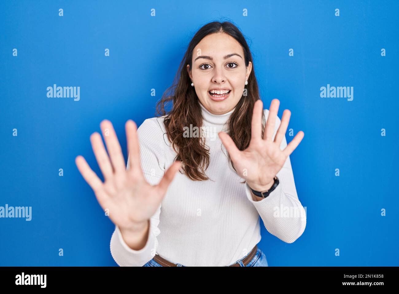 Young hispanic woman standing over blue background afraid and terrified ...