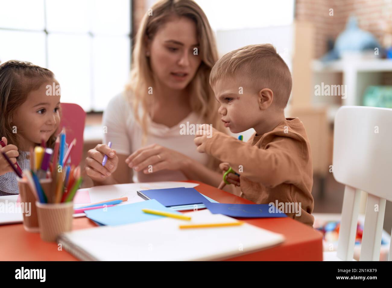 Teacher with boy and girl sitting on table having handcrafts class at ...