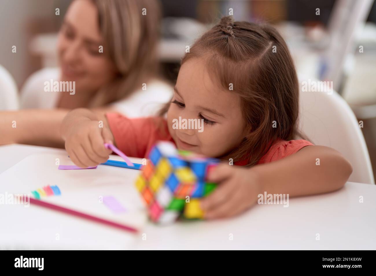 Teacher and toddler sitting on table holding rubik cube at kindergarten ...