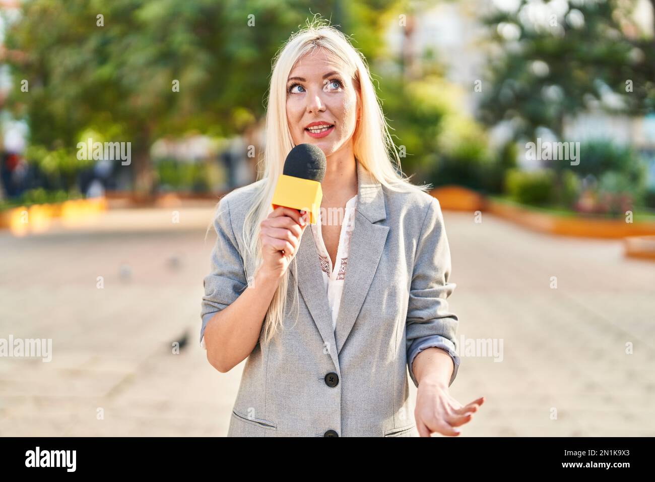 Young blonde woman reporter working using microphone at park Stock ...