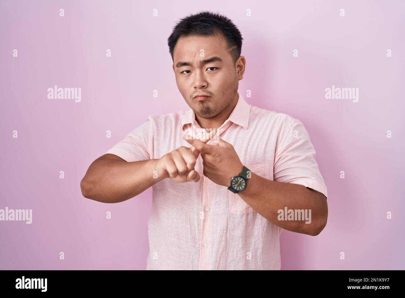 Chinese young man standing over pink background rejection expression ...
