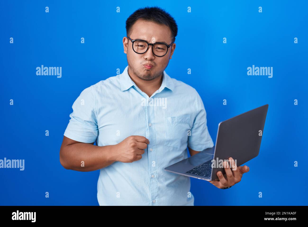 Chinese young man using computer laptop puffing cheeks with funny face ...