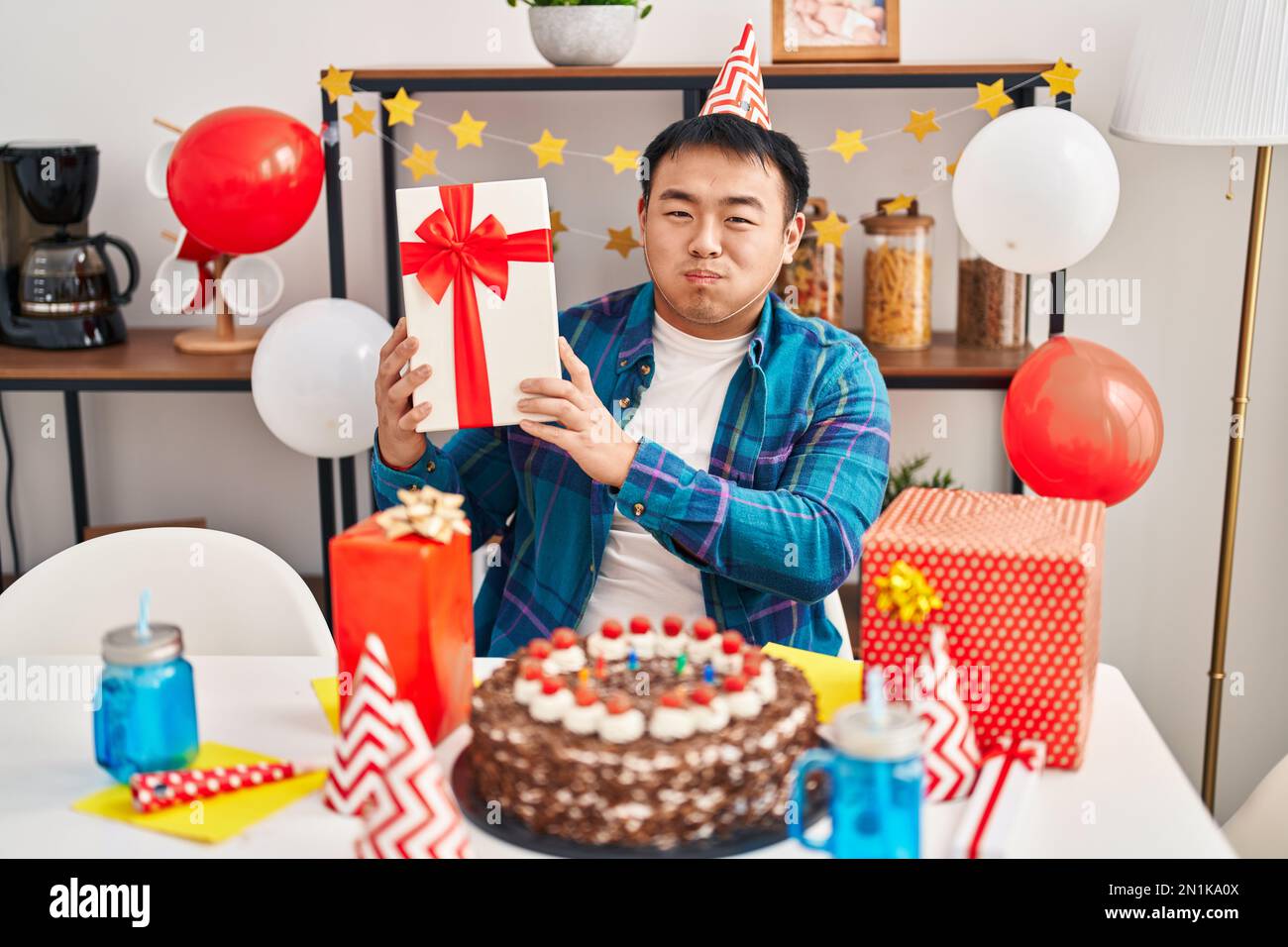 Young chinese man celebrating birthday with cake and present puffing ...