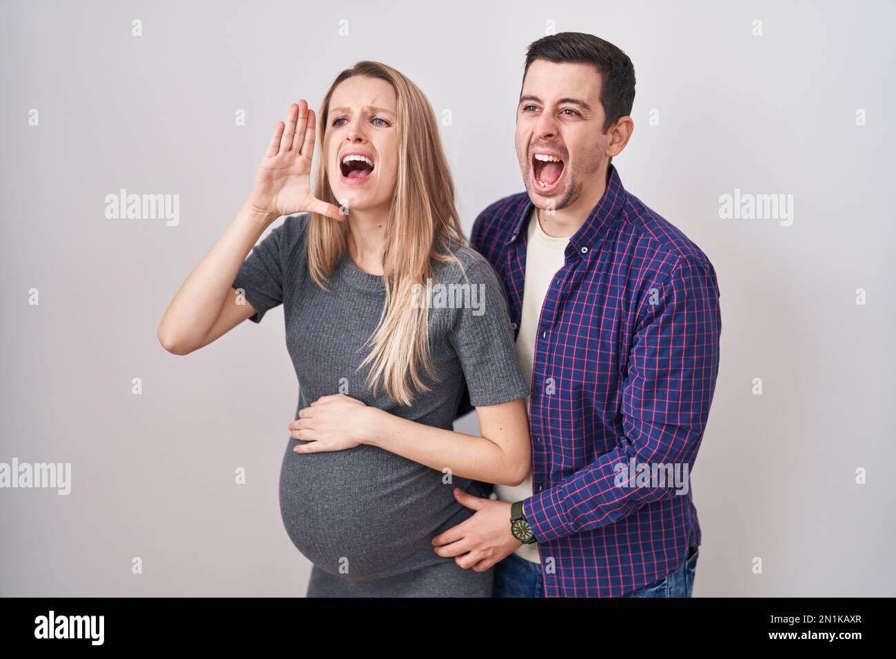 Young couple expecting a baby standing over white background shouting ...