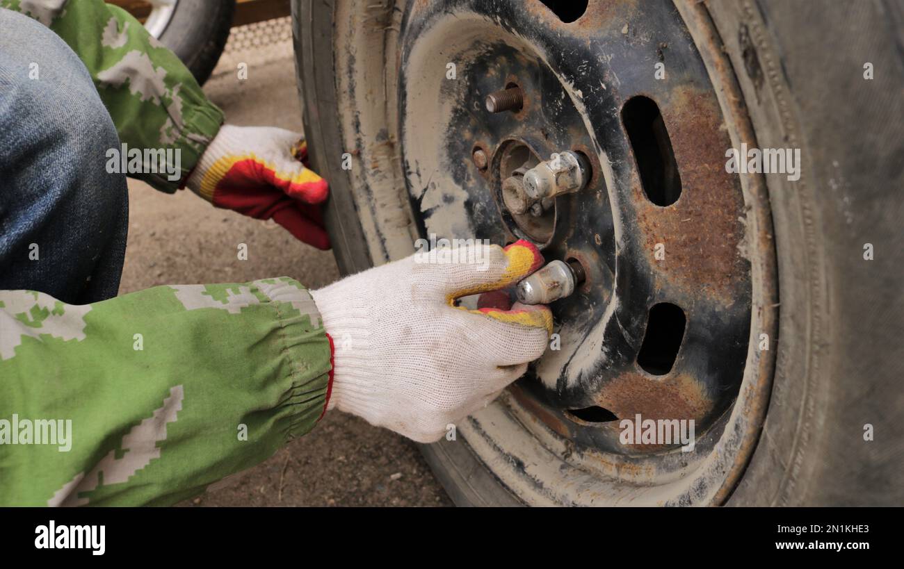hands of an auto mechanic in gloves put a nut on a stud in the ...