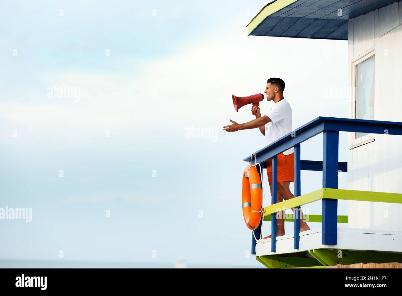 Male lifeguard with megaphone on watch tower against blue sky Stock ...