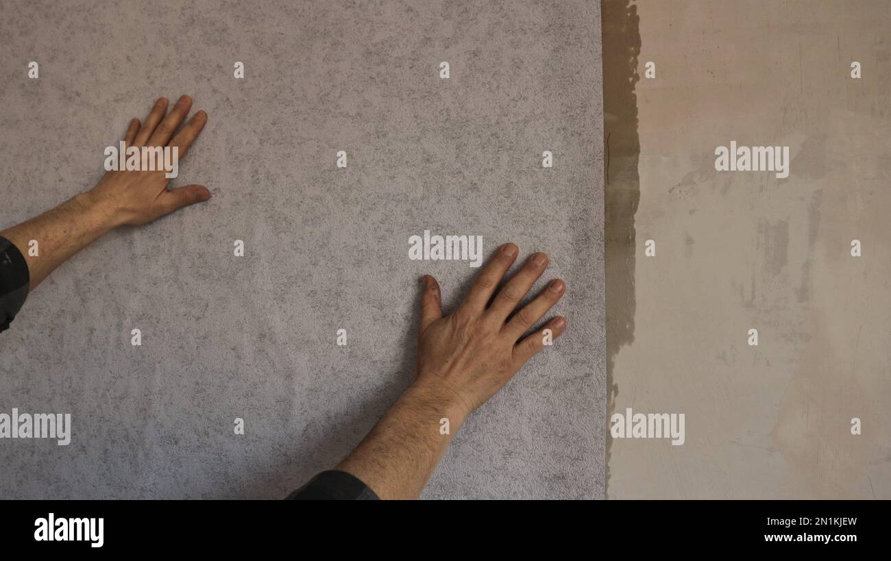 male hands touch the wall with a layer of glue applied and stick a ...